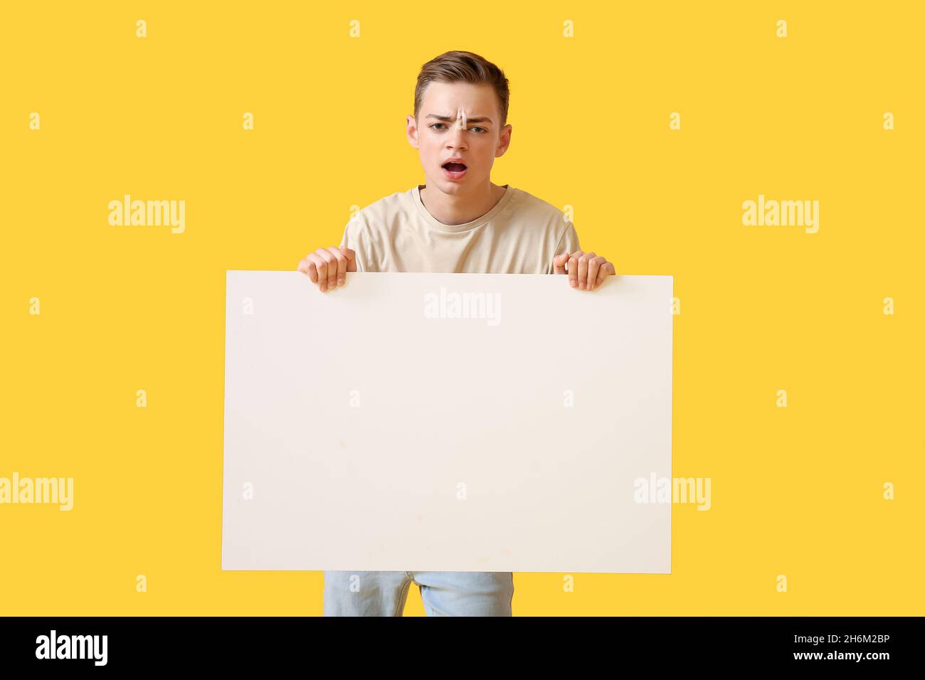 Shocked teenage boy with blank poster on yellow background Stock Photo ...