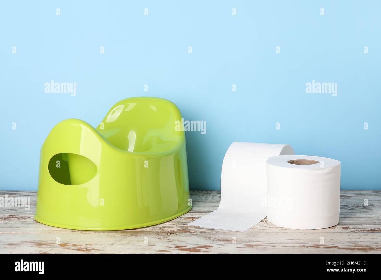 Modern potty and toilet paper rolls on wooden floor near color wall ...