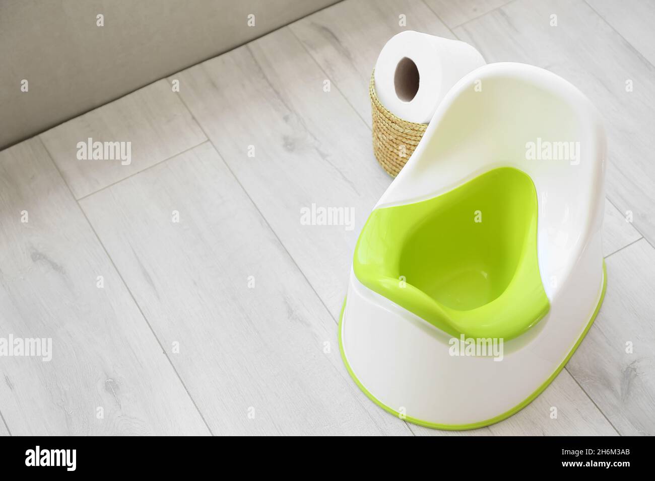 White potty and basket with toilet paper roll on grey wooden floor ...