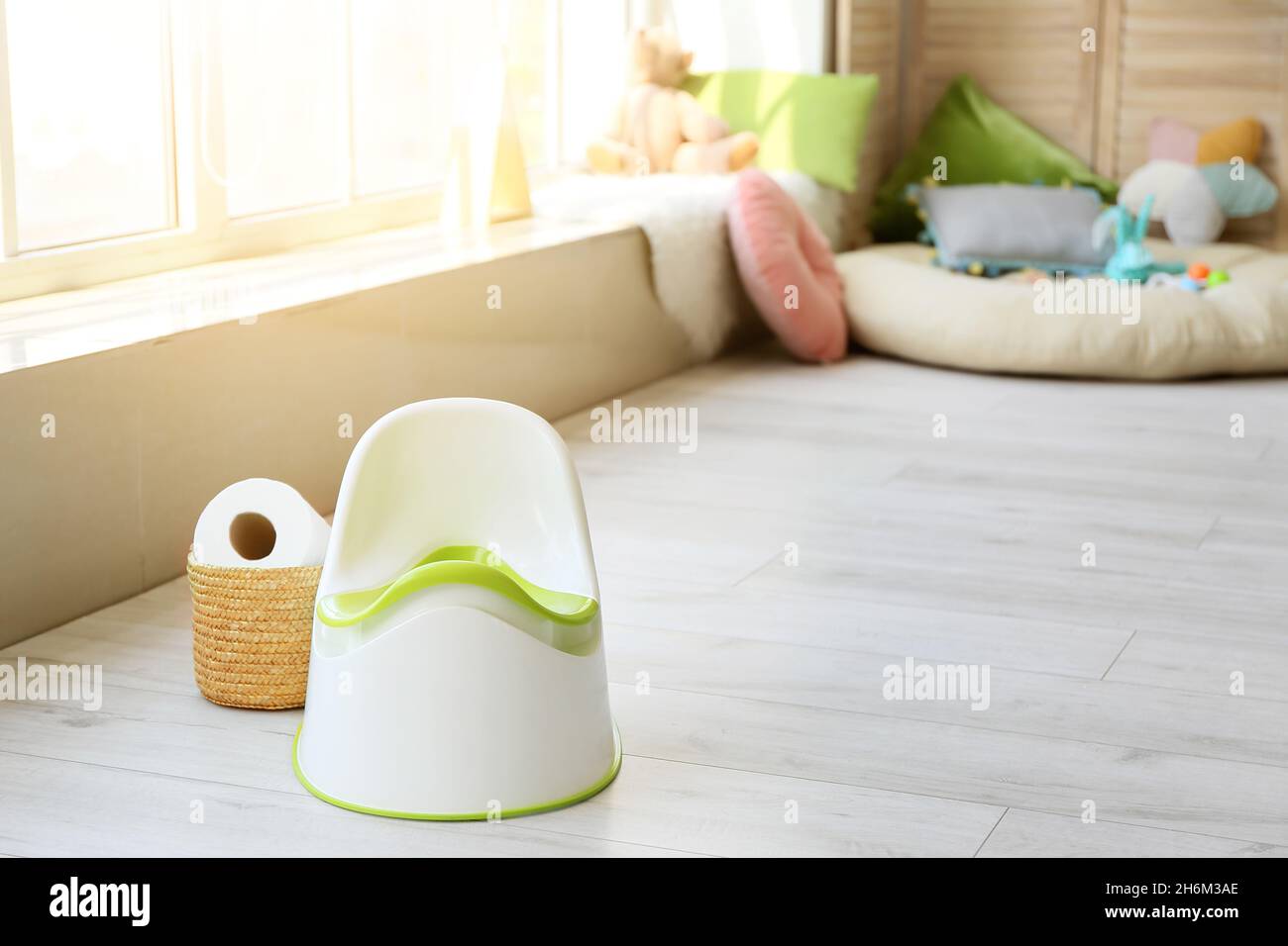 White potty and basket with toilet paper roll on wooden floor in light ...