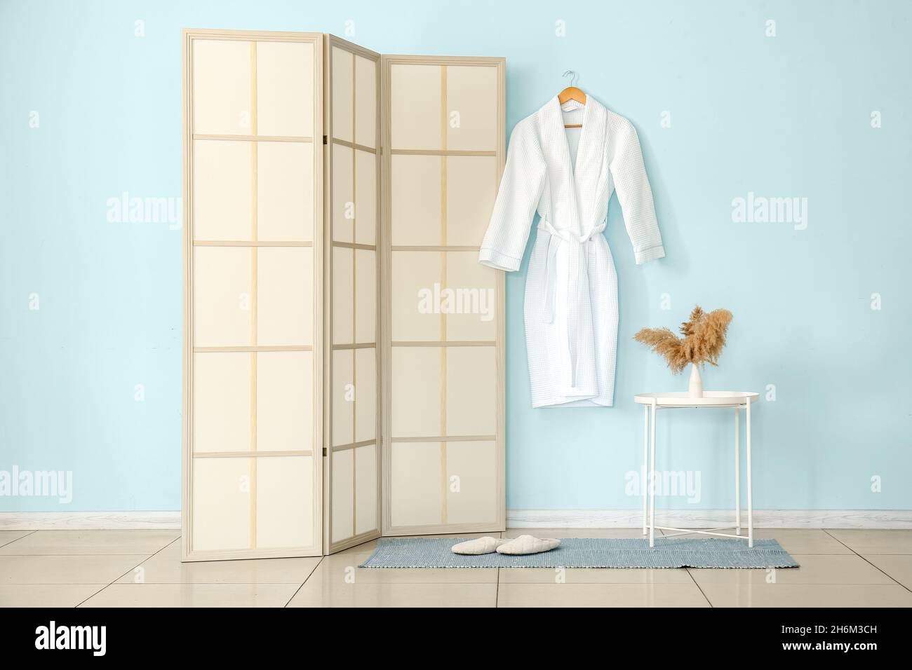 Folding screen, bathrobe and table with vase near blue wall Stock Photo ...