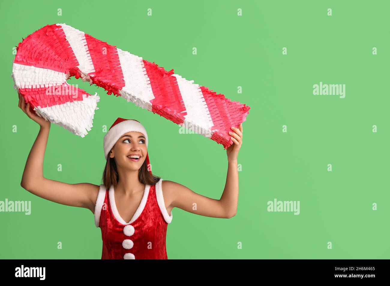 Beautiful woman dressed as Santa with candy cane pinata on color ...