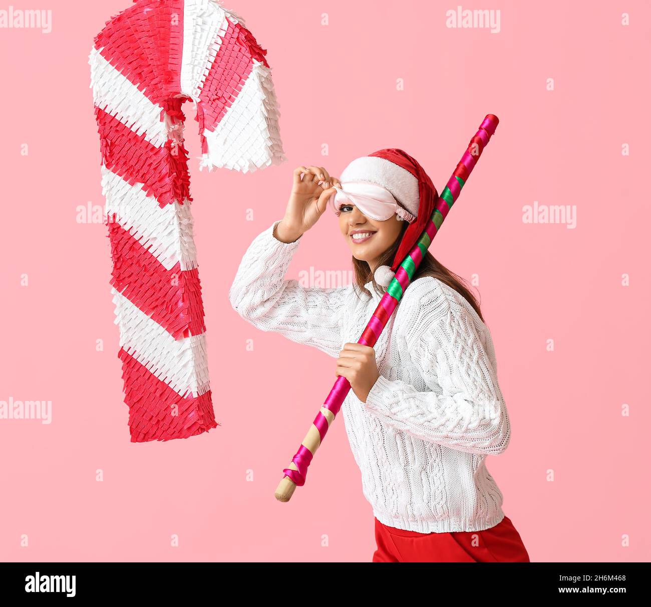 Beautiful woman in Santa hat and with candy cane pinata on color ...