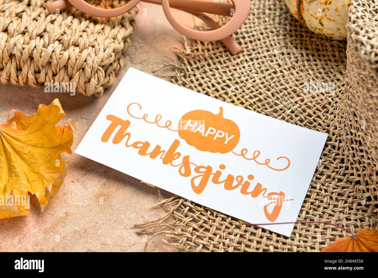 Wicker hat, dry leaves and paper card with text HAPPY THANKSGIVING on ...