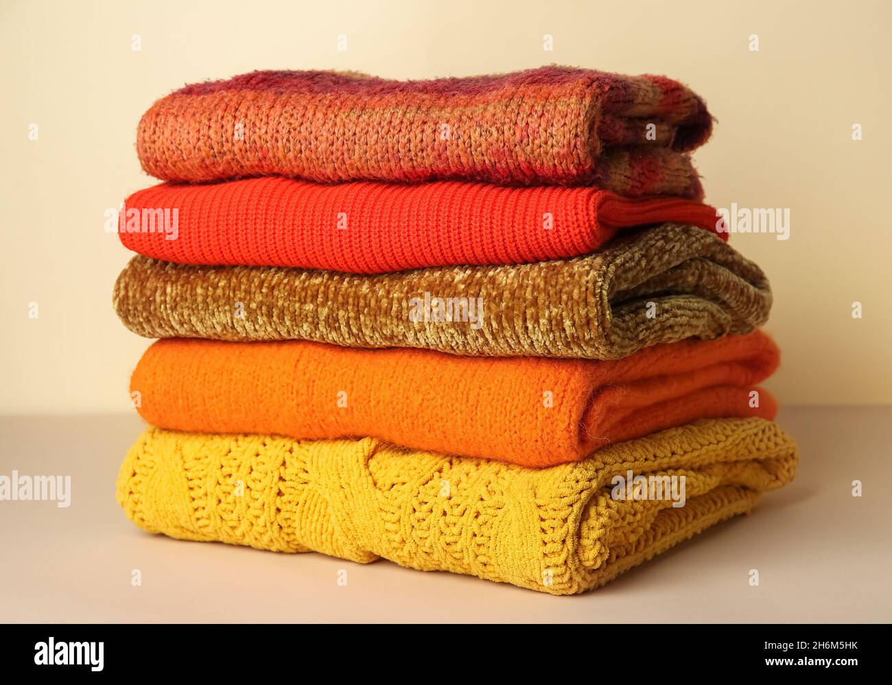 Stack of different stylish sweaters on table against color background ...