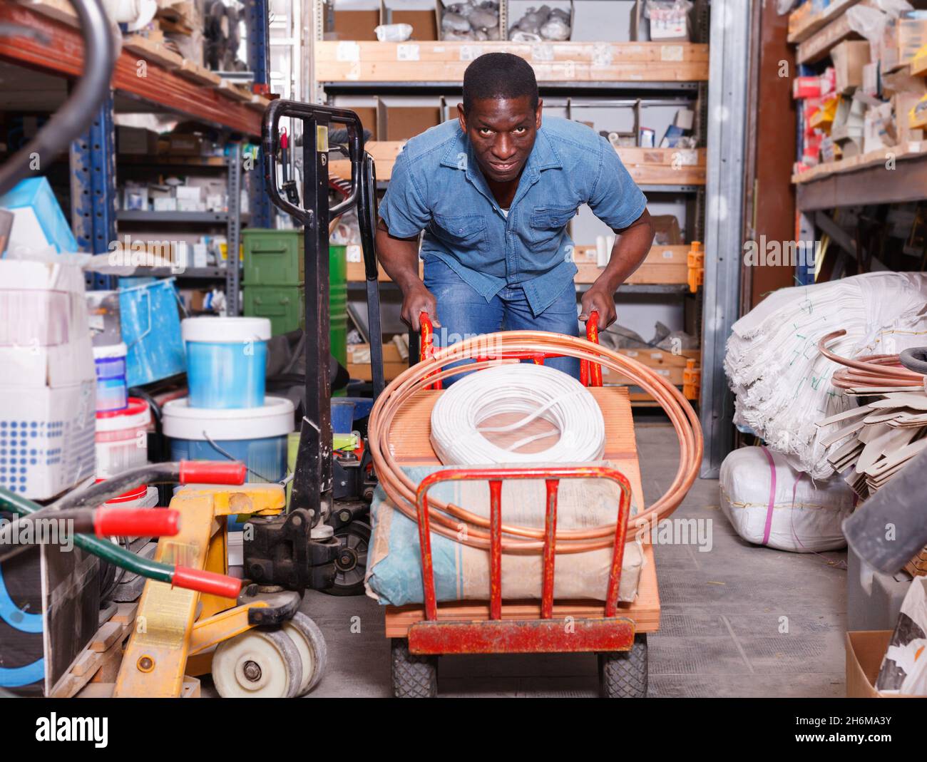 Focused African American carrying handbarrow with construction supplies ...
