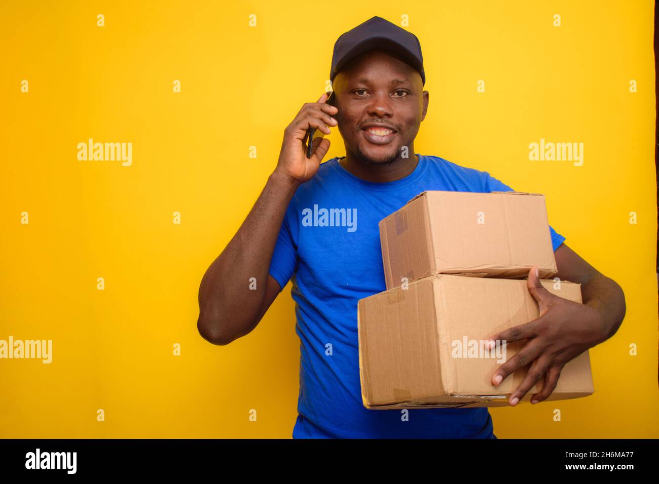 African dispatch man making a call with a smartphone, carrying boxes ...