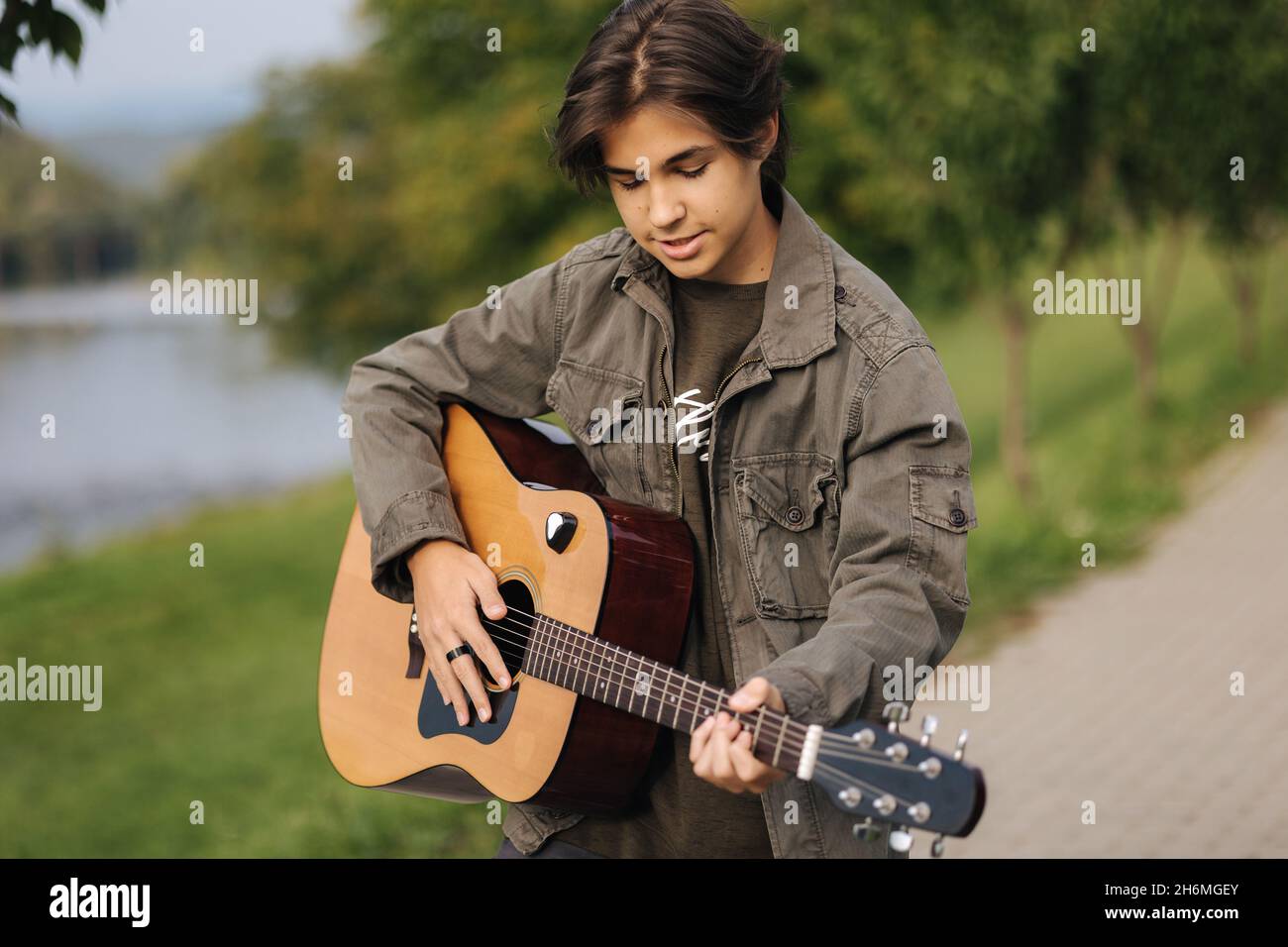 Concentrated teenage boy musician playing acoustic guitar outdoor ...