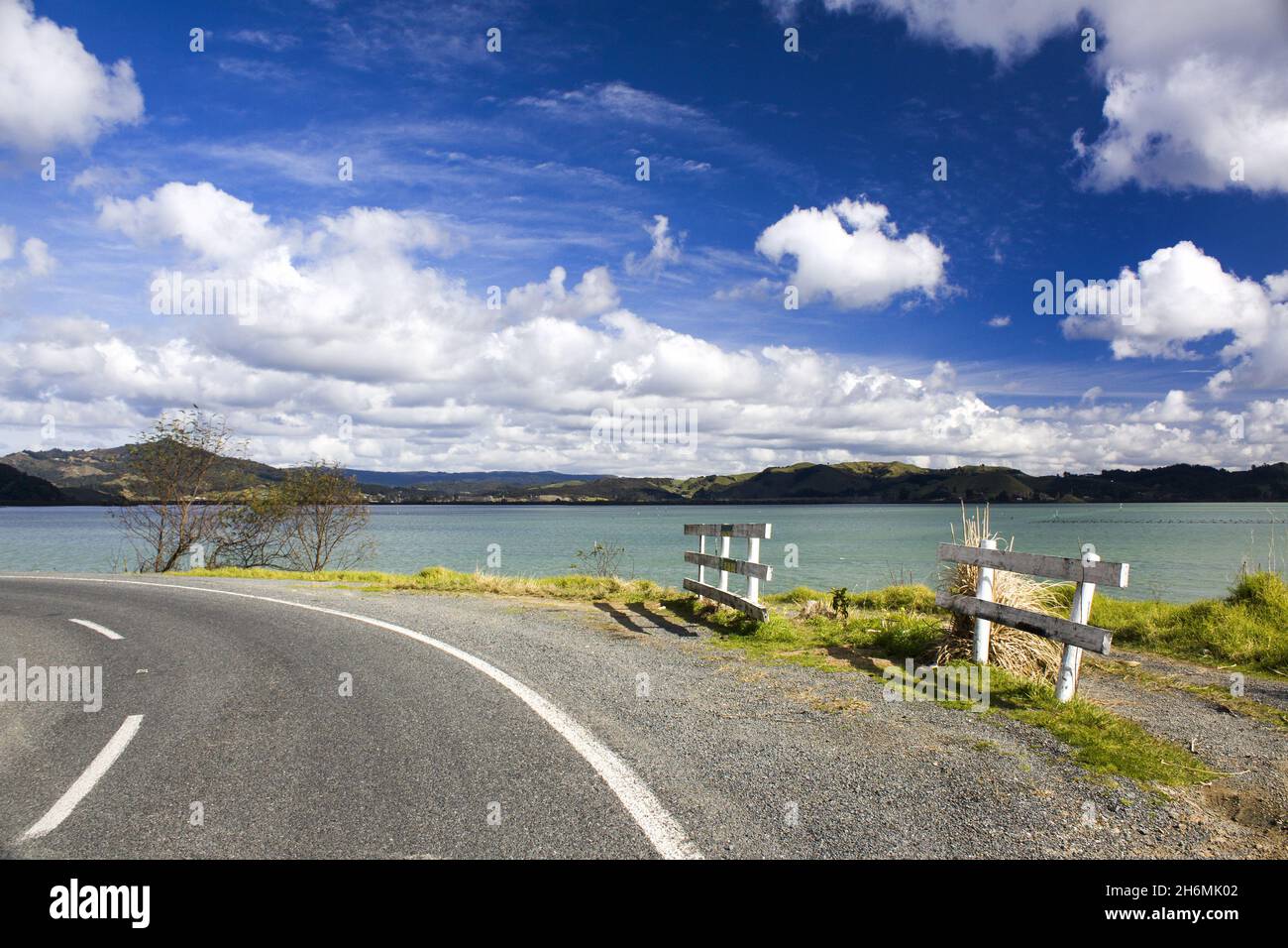 Curvy road surrounded by a lake under a blue cloudy sky in New Zeal ...