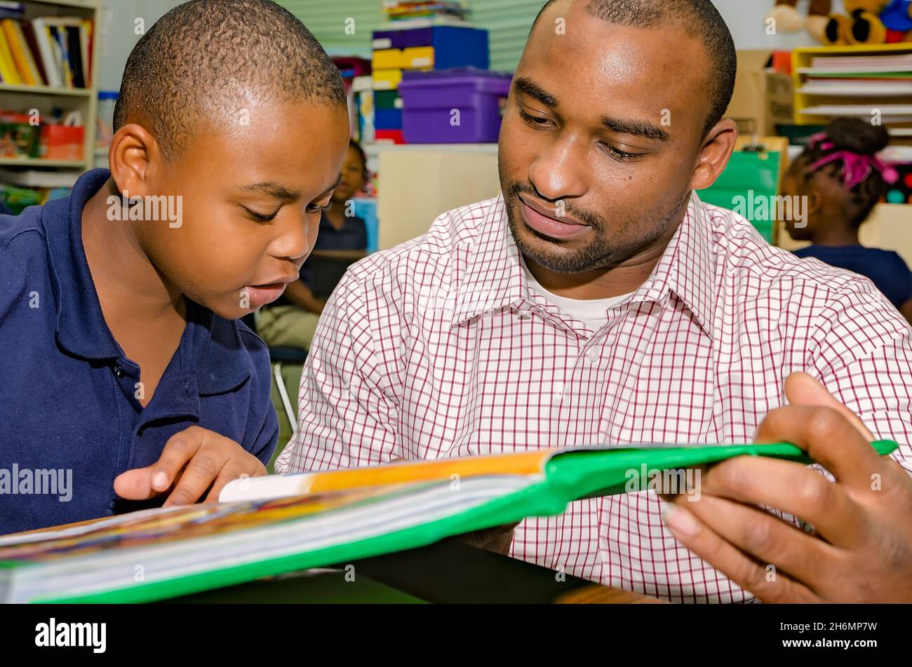 A male teacher helps an elementary school student with a reading lesson ...