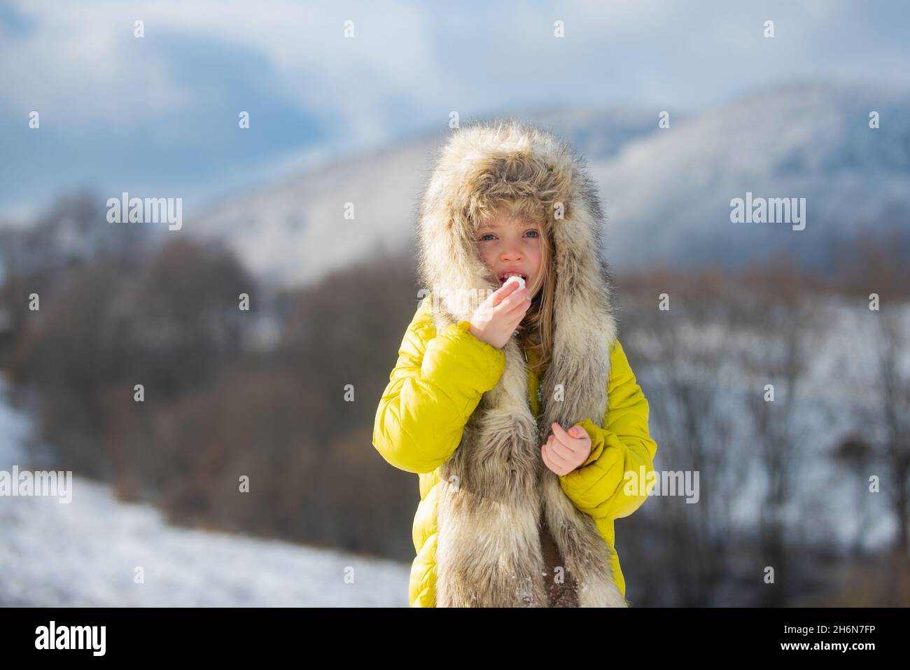 Funny child, cute girl eating snow and playing in winter snowy park ...