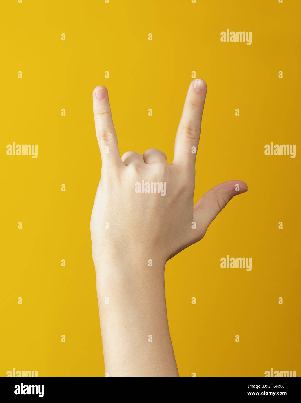 hand showing rock and roll gesture on yellow background. Hand makes ...