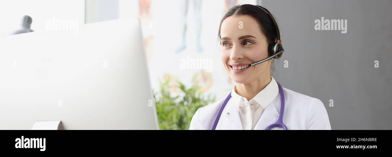 Doctor in headphones with microphone holding x ray in front of computer ...