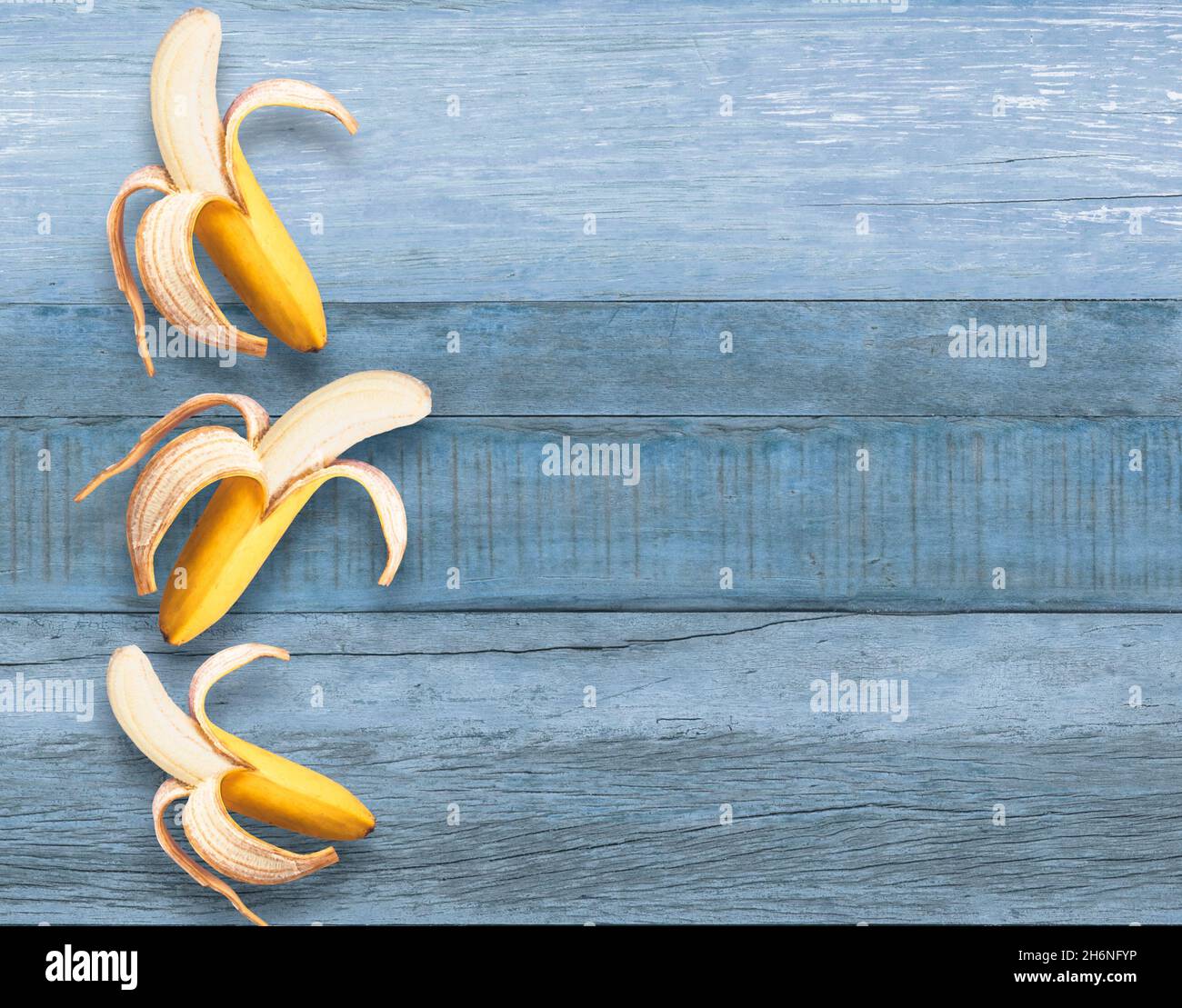 Half-opened bananas in a row on a left side of a blue wooden background ...