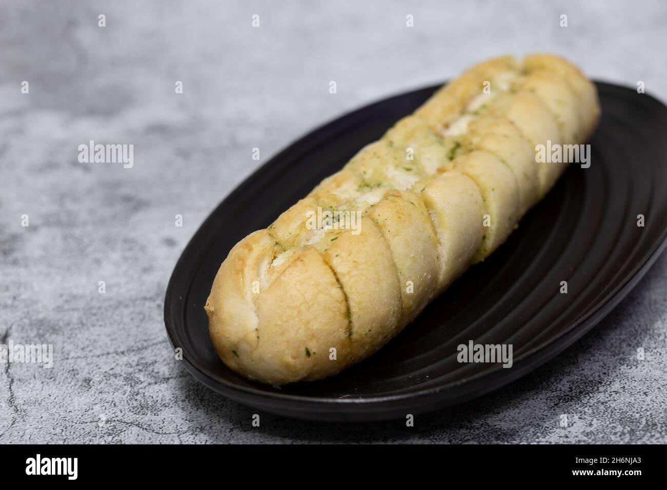 Cheesy garlic bread baton baguette with herbs on a black granite plate ...