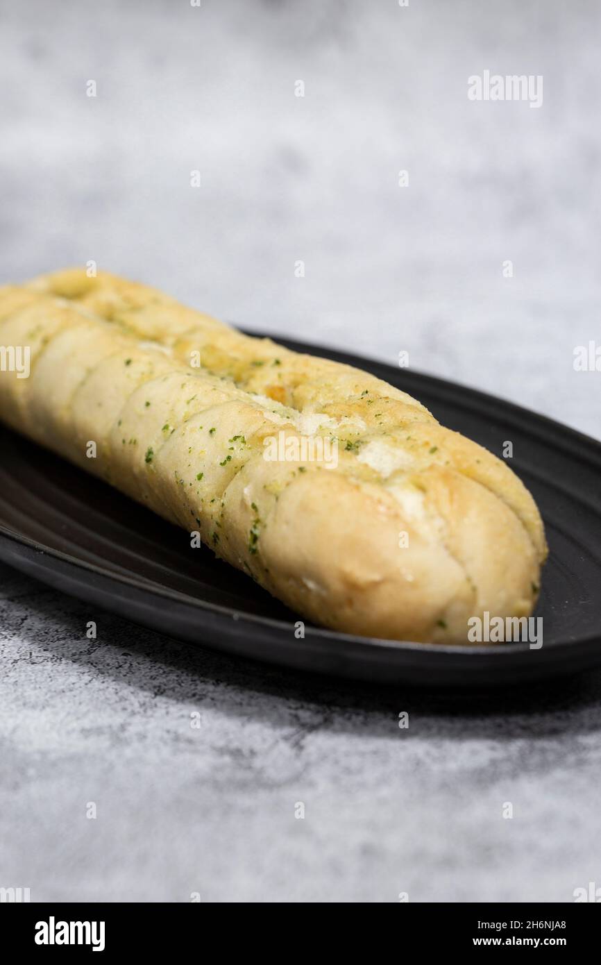 Cheesy garlic bread baton baguette with herbs on a black granite plate ...