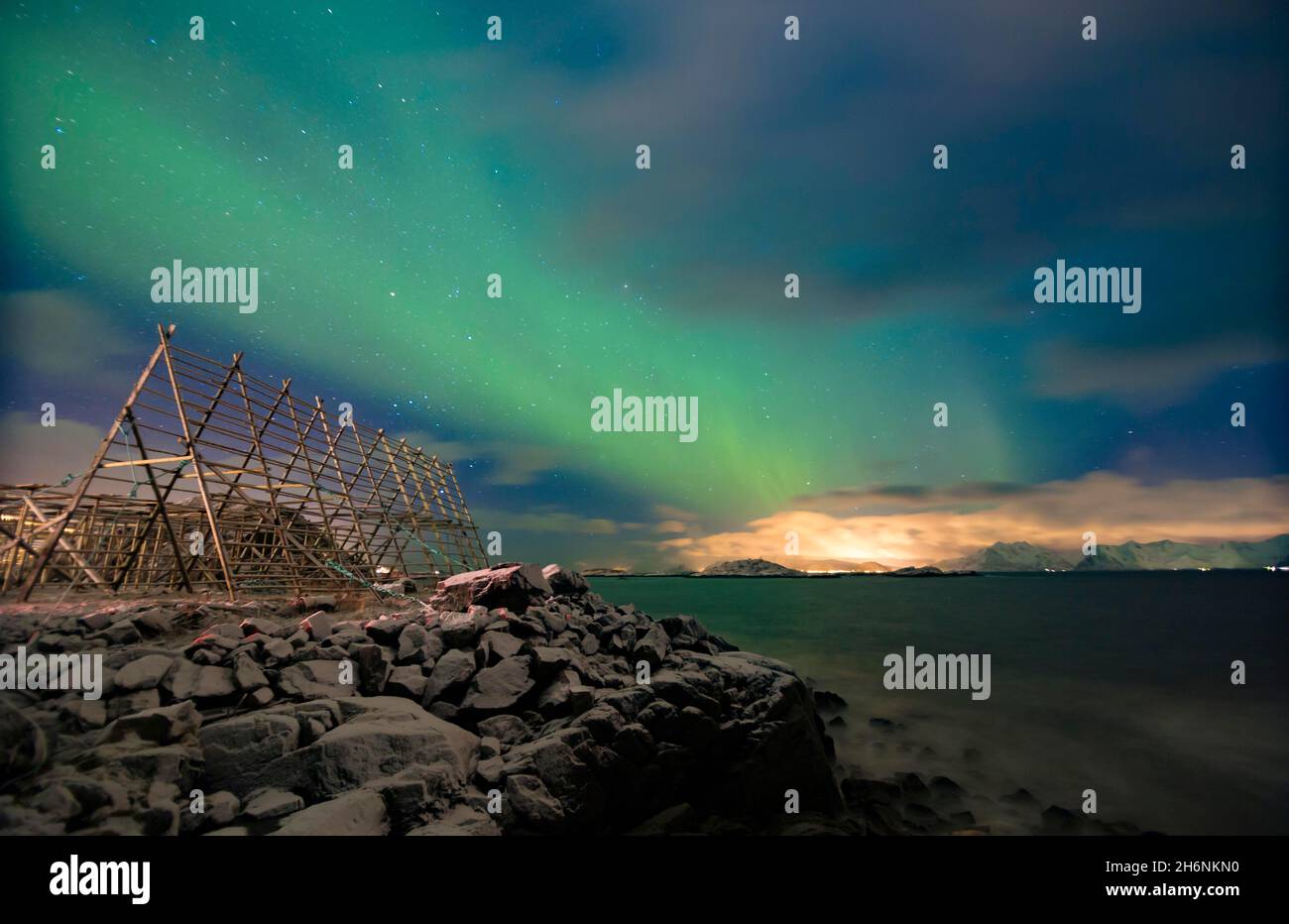 Aurora borealis over a worker in a wooden stockfish rack, Svolvaer ...