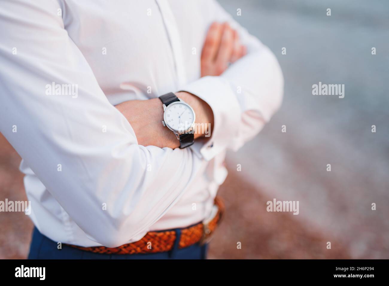 Man in a white shirt with a watch on his wrist crossed his arms over ...