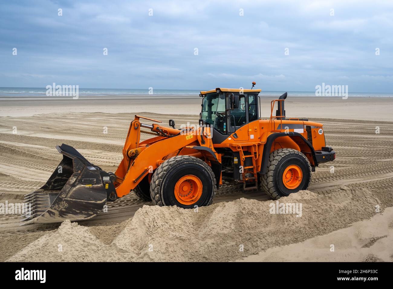 orange bulldozer is moving sand at the beach of Berck sur mer in ...
