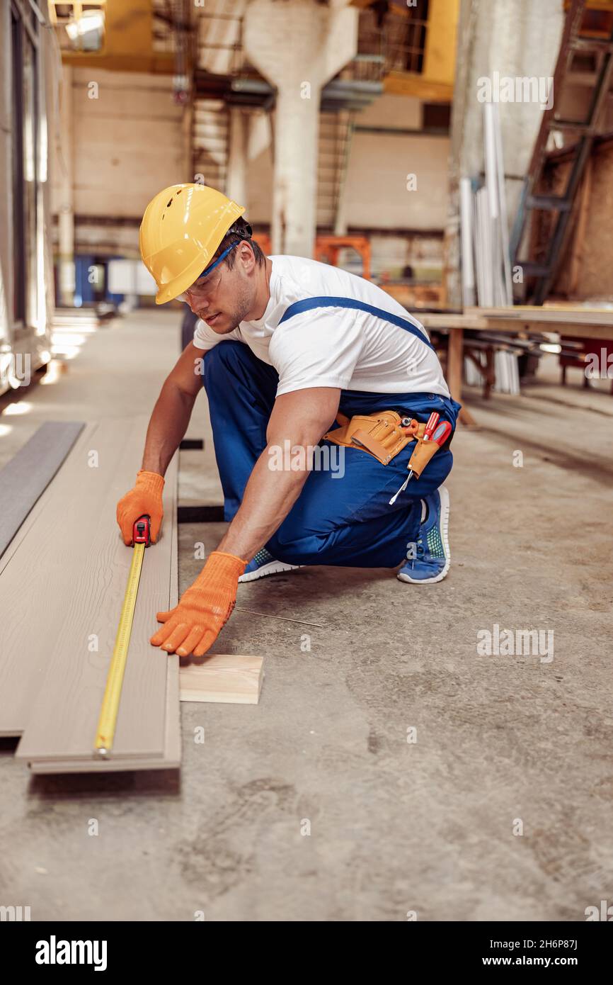 Male builder measuring timber plank at construction site Stock Photo ...