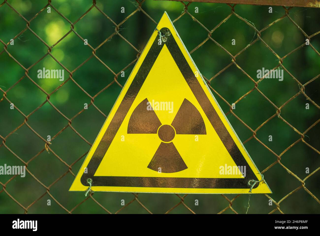 Close-up of a yellow triangular radiation sign on a wire mesh. In the ...