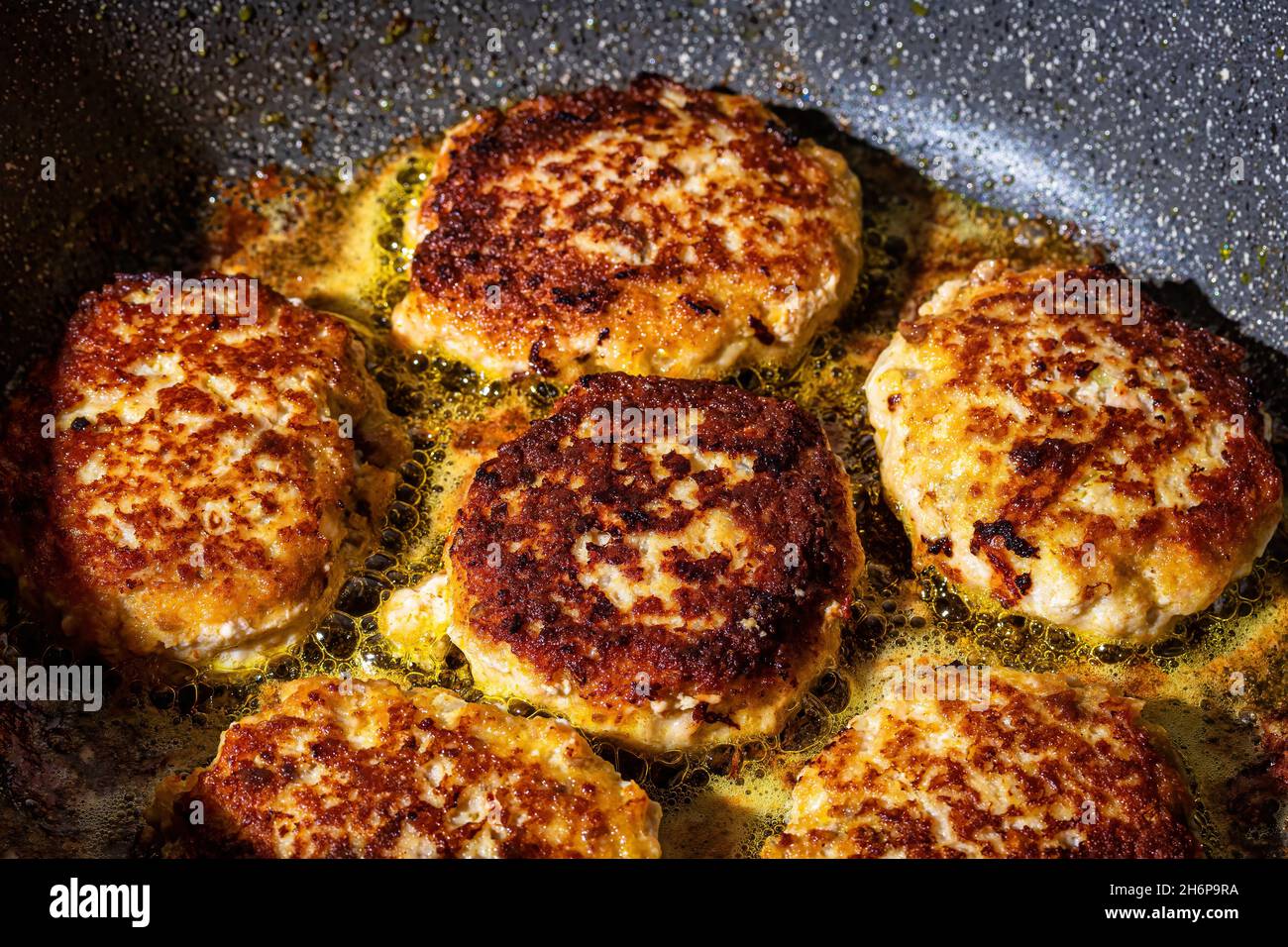 Raw white fish meat cutlets, heated in a ceramic black skillet with ...