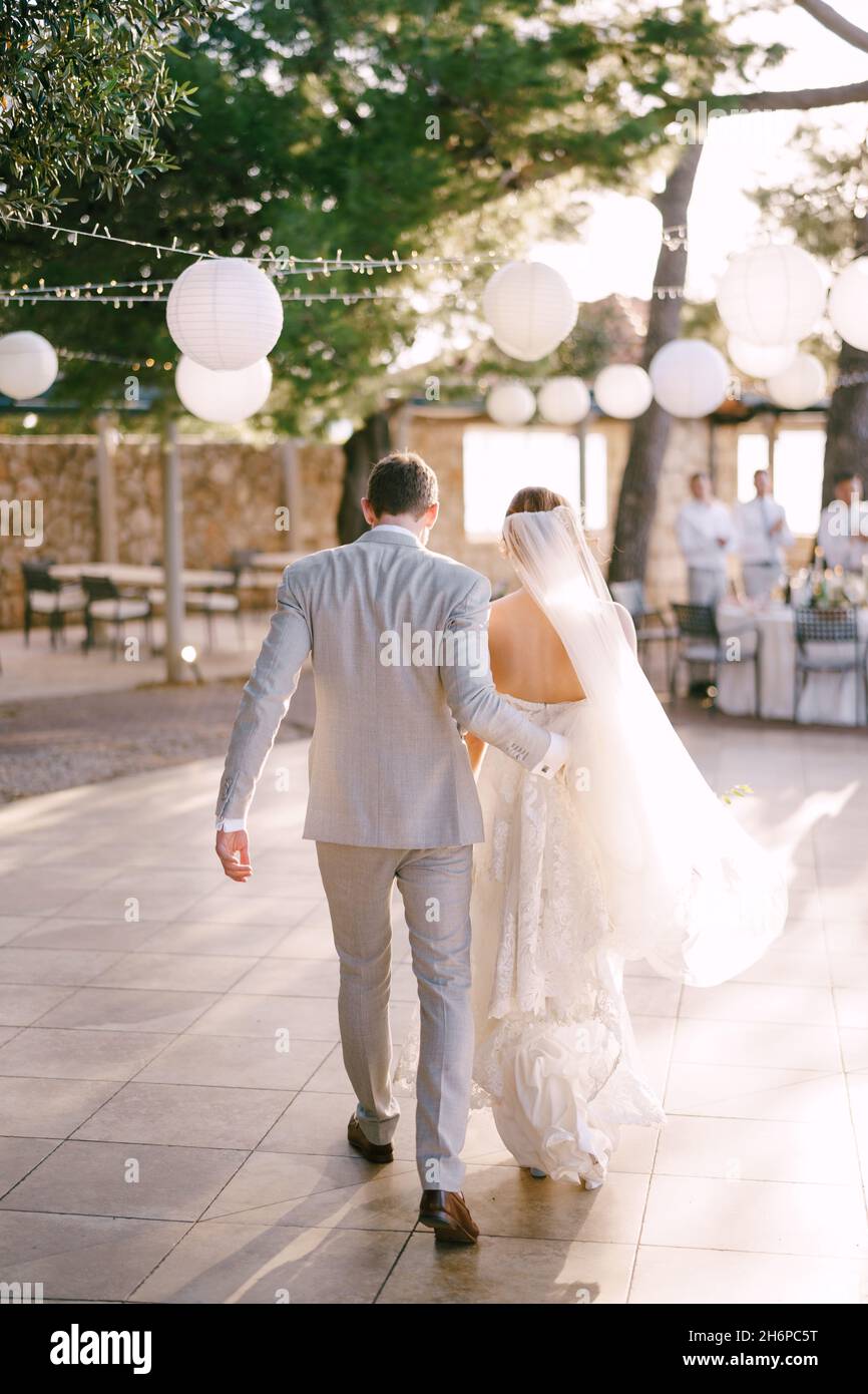 Bride and groom walk along the restaurant terrace to the table with ...