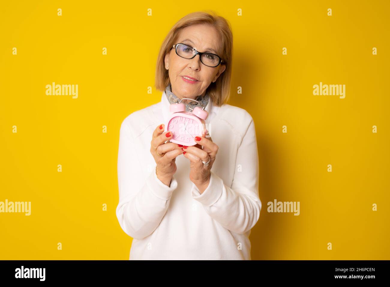 Mature woman showing clock isolated over yellow background Stock Photo ...