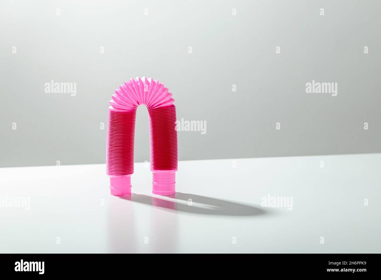 Pink antistress pop tube toy in shape of arch on light background with ...