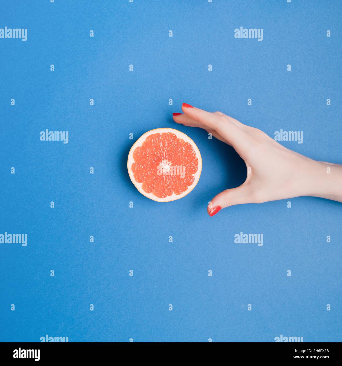 Female hand with red nails reaching towards bright grapefruit slice ...