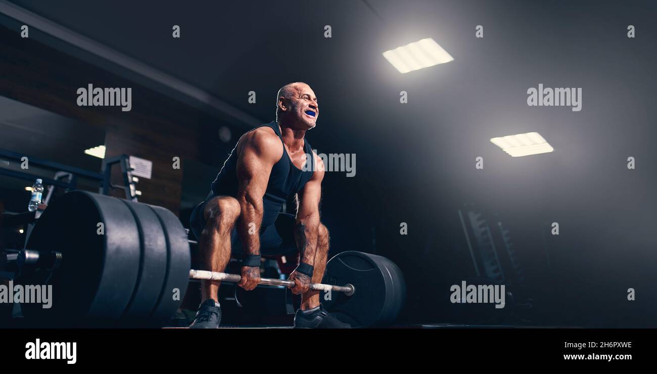 Emotional older powerlifter preparing to exercise deadlift with barbell ...