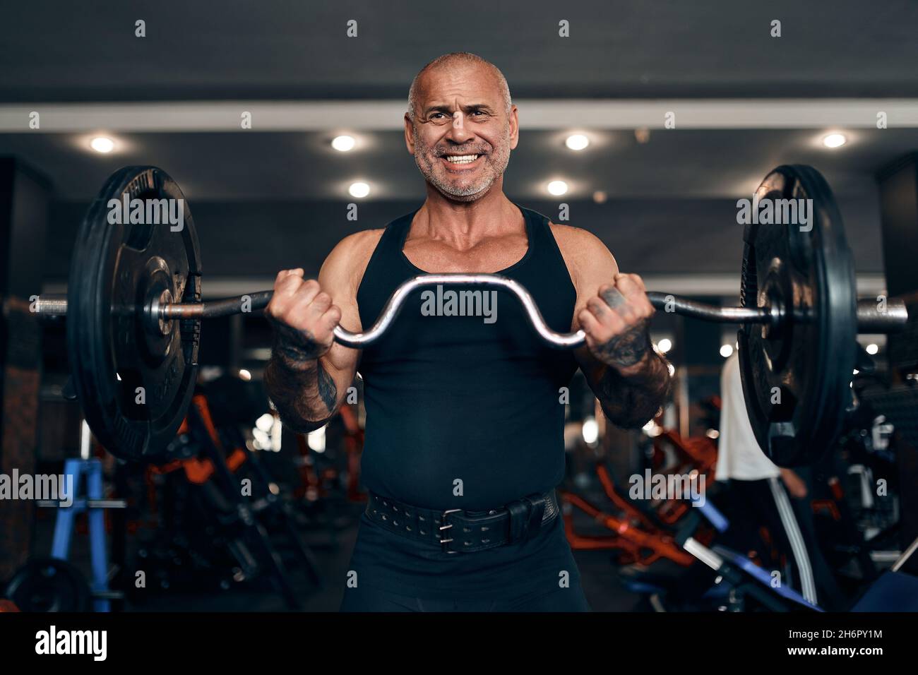 Front view of bodybuilder who doing exercises with barbell at biceps in ...