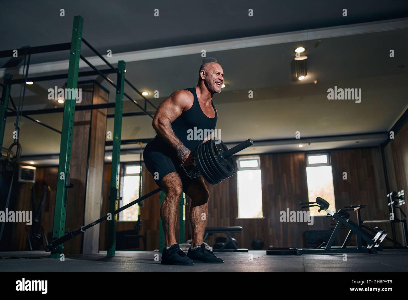 Strong adult caucasian bald weightlifter works out with heavy barbell ...