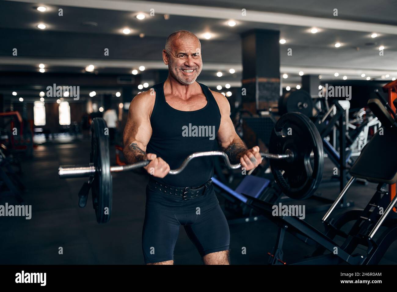 Muscular older man working out in gym doing exercises with barbell at ...