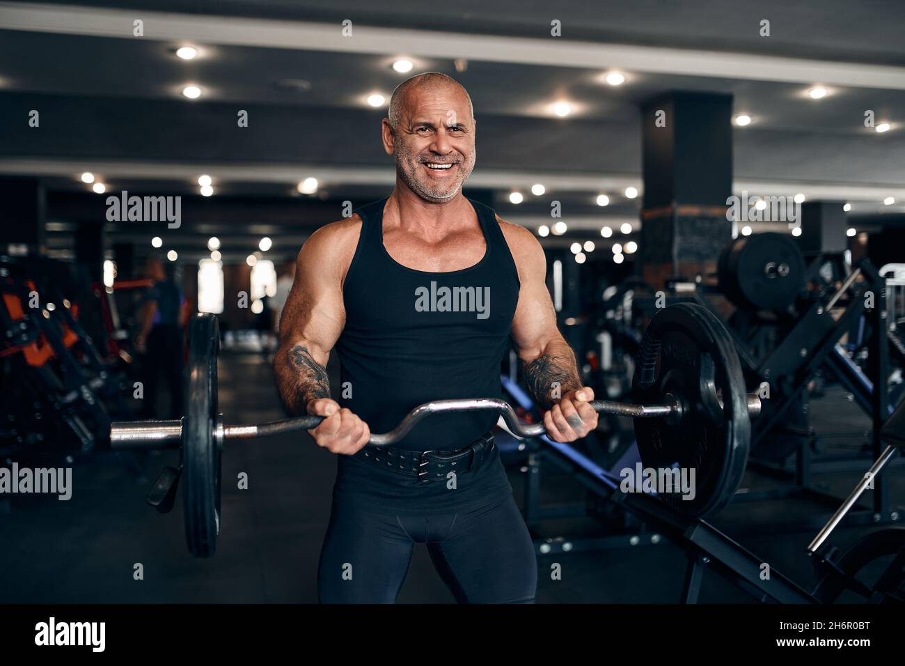 Muscular bald man working out in gym doing exercises with barbell at ...