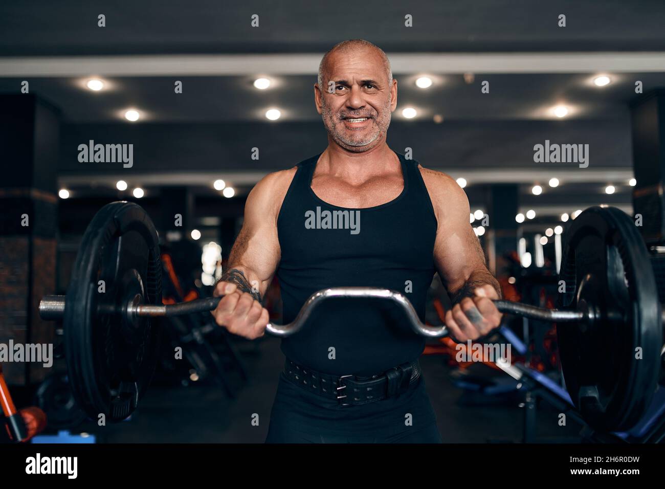 Front view of older bodybuilder doing exercises with barbell at biceps ...