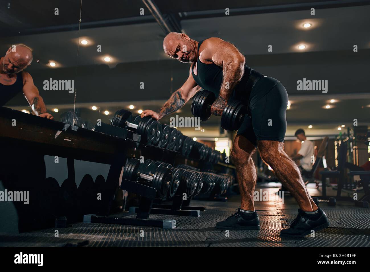 Bald male bodybuilder doing exercises with dumbbells while posing in ...