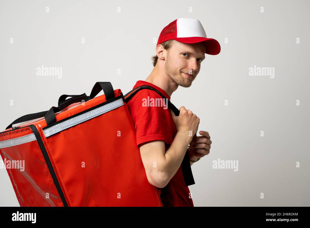 Side view delivery employee man 20s in red cap t-shirt uniform thermal ...