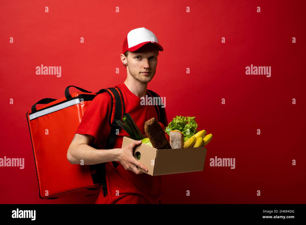 Delivery man in red uniform holds craft cardboard box with food ...
