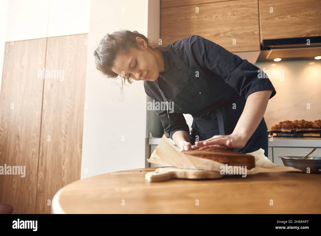 young professional female cook is preparing tasty cake at her light ...