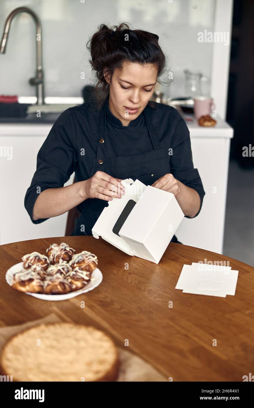 young professional female cook is preparing tasty cake at her light ...