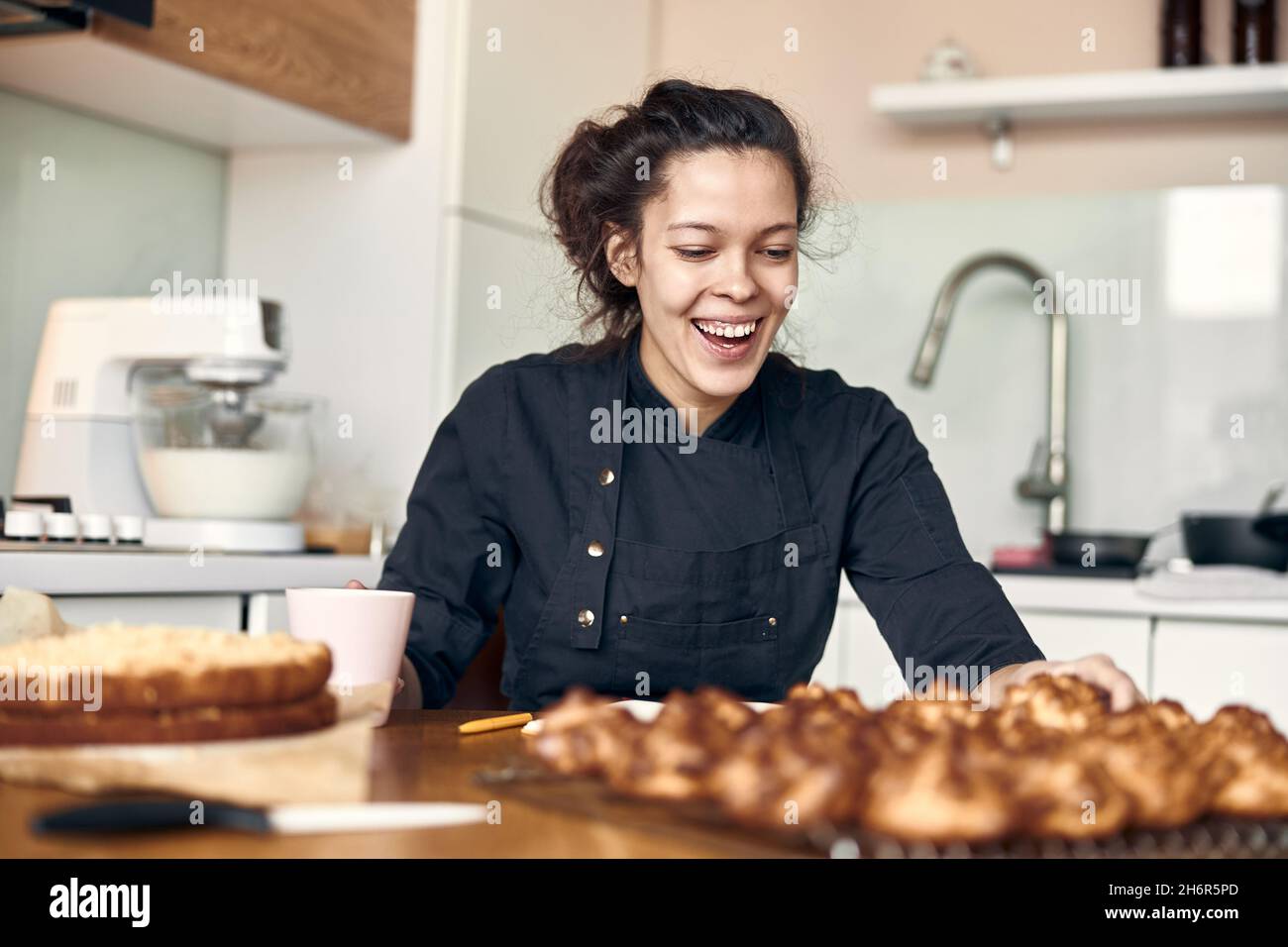 young professional female cook is preparing tasty cake at her light ...