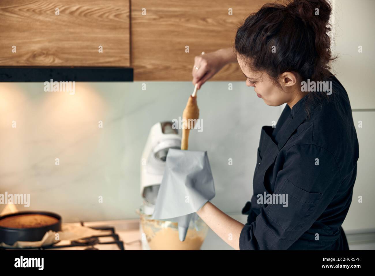 beautiful caucasian lady cook is making eclairs with help of pastry ...