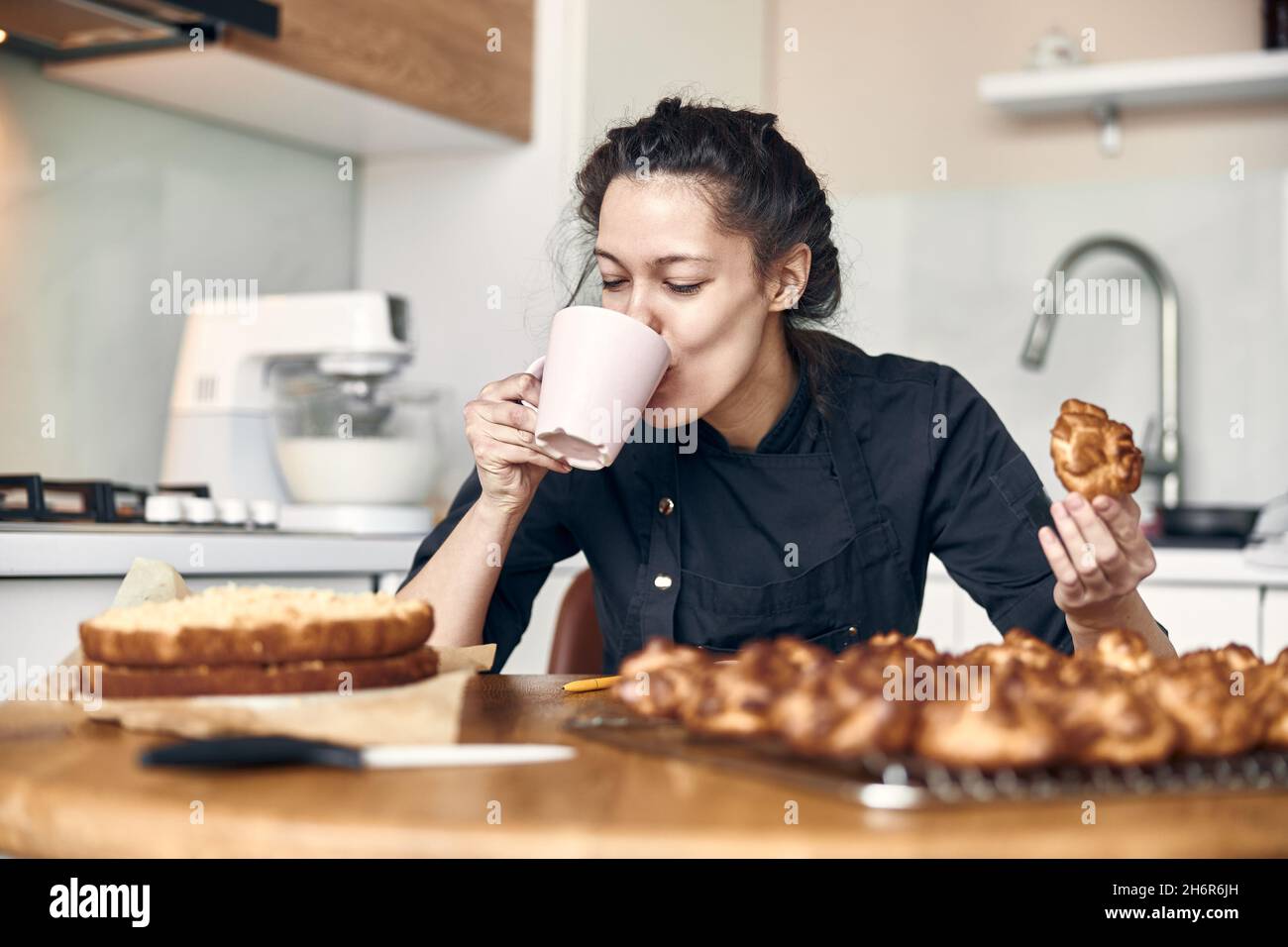 young professional female cook is preparing tasty cake at her light ...