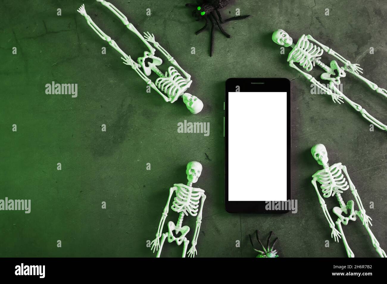 Skeletons around a smartphone with a white display on a dark background ...