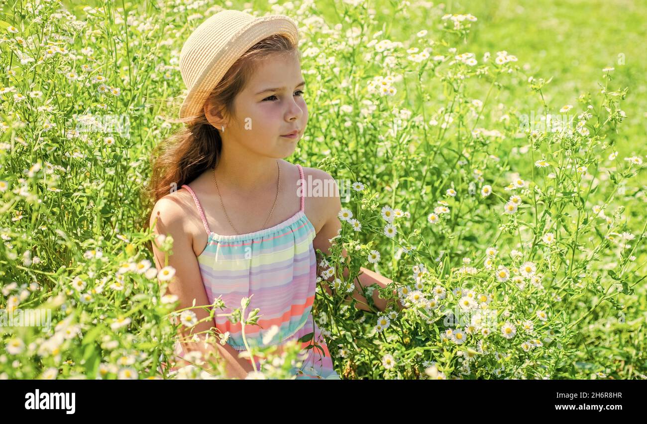 Little child with beauty look wear sun hat relaxing on chamomile flower ...