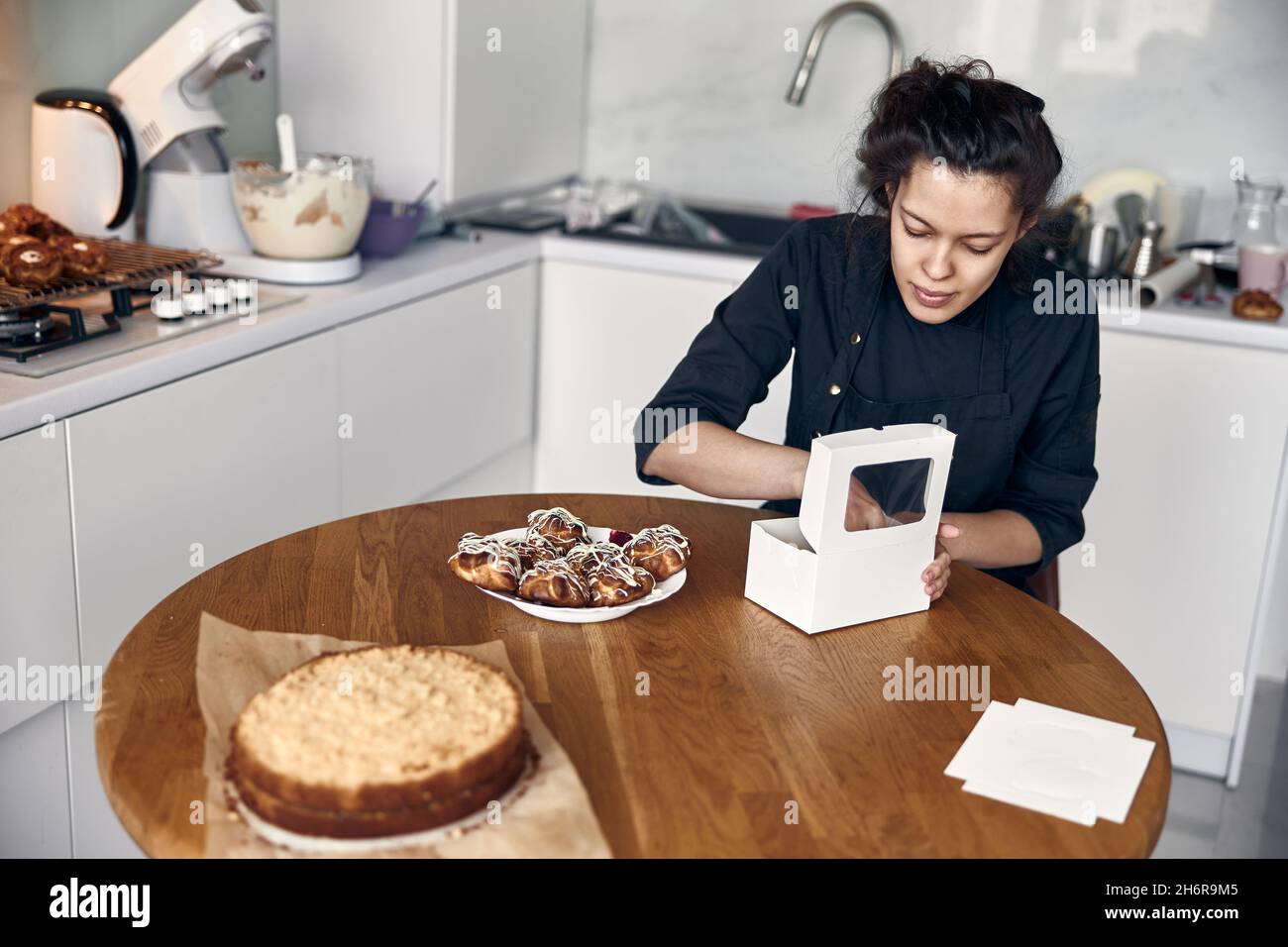 young professional female cook is preparing tasty cake at her light ...