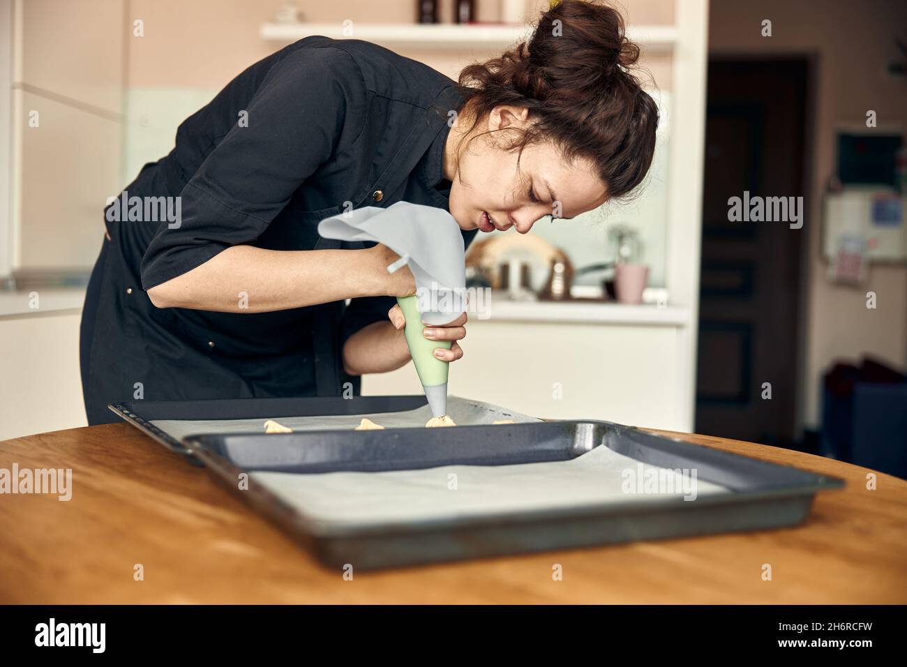 beautiful caucasian lady cook is making eclairs with help of pastry ...