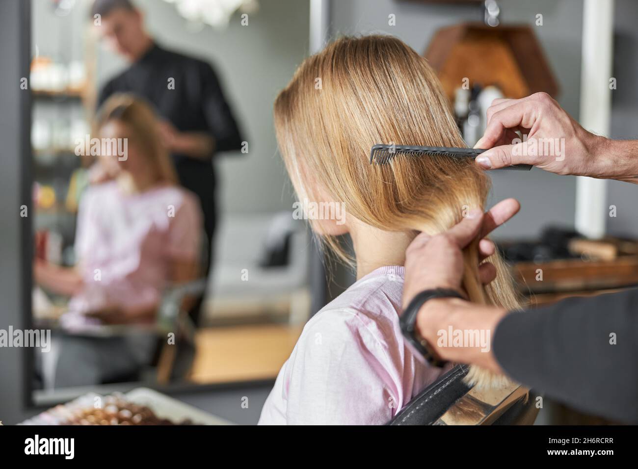Pofessional hairdresser is combing a hair of beautiful caucasian blonde ...