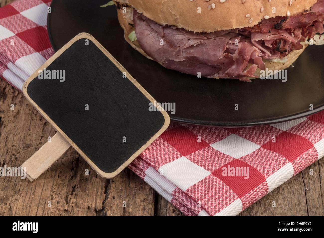 A delicious roast beef burger and an empty chalkboard on wooden table ...